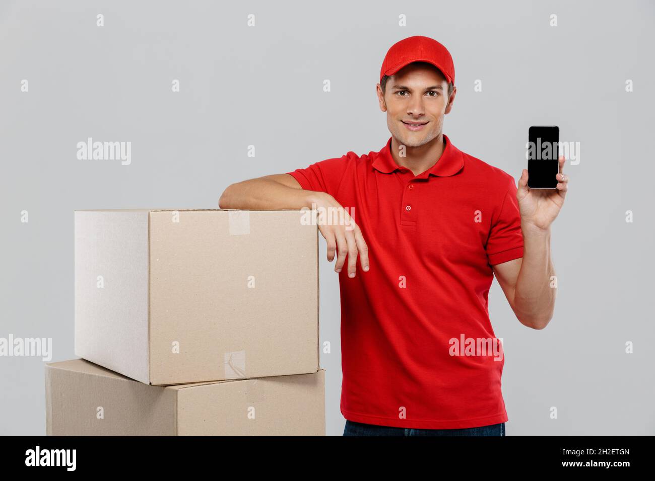 Young delivery man showing cellphone while posing with cardboard boxes ...