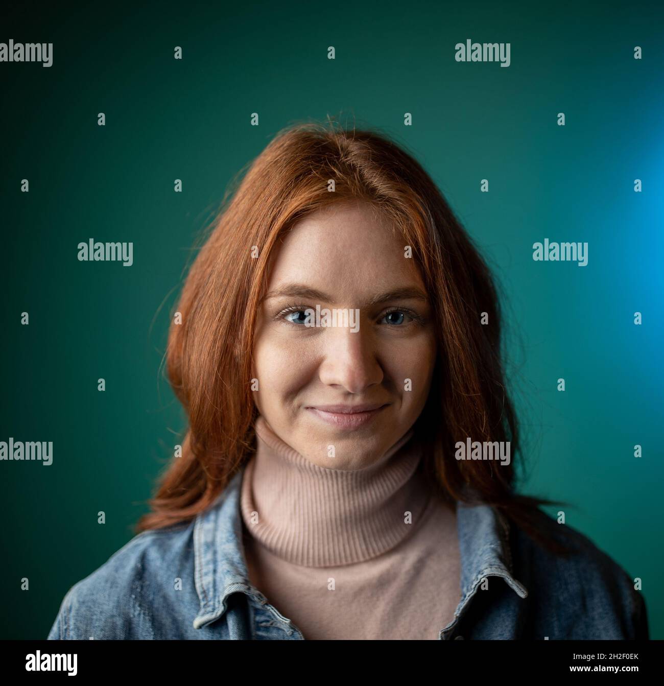 Portrait of modest red hair young woman with blue eyes against color ...