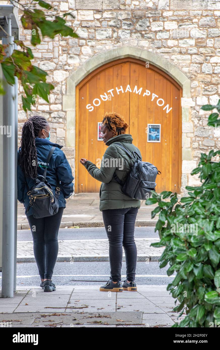 two black or B A M E women females talking standing at a bus stop or ...