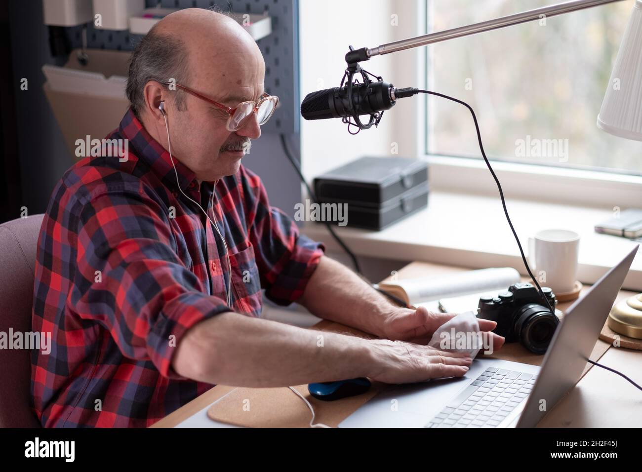 Senior man at home in front of laptop computer wiping dust from laptop ...