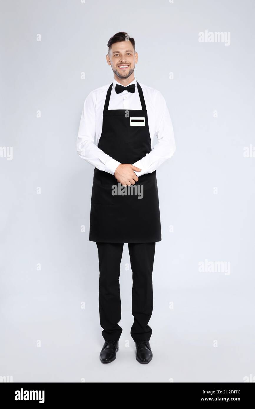 Full length portrait of handsome waiter in elegant uniform on light ...