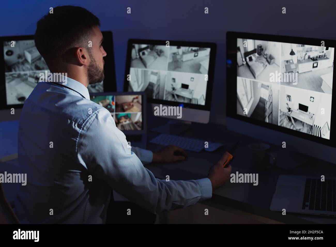 Male security guard with portable transmitter monitoring home cameras ...