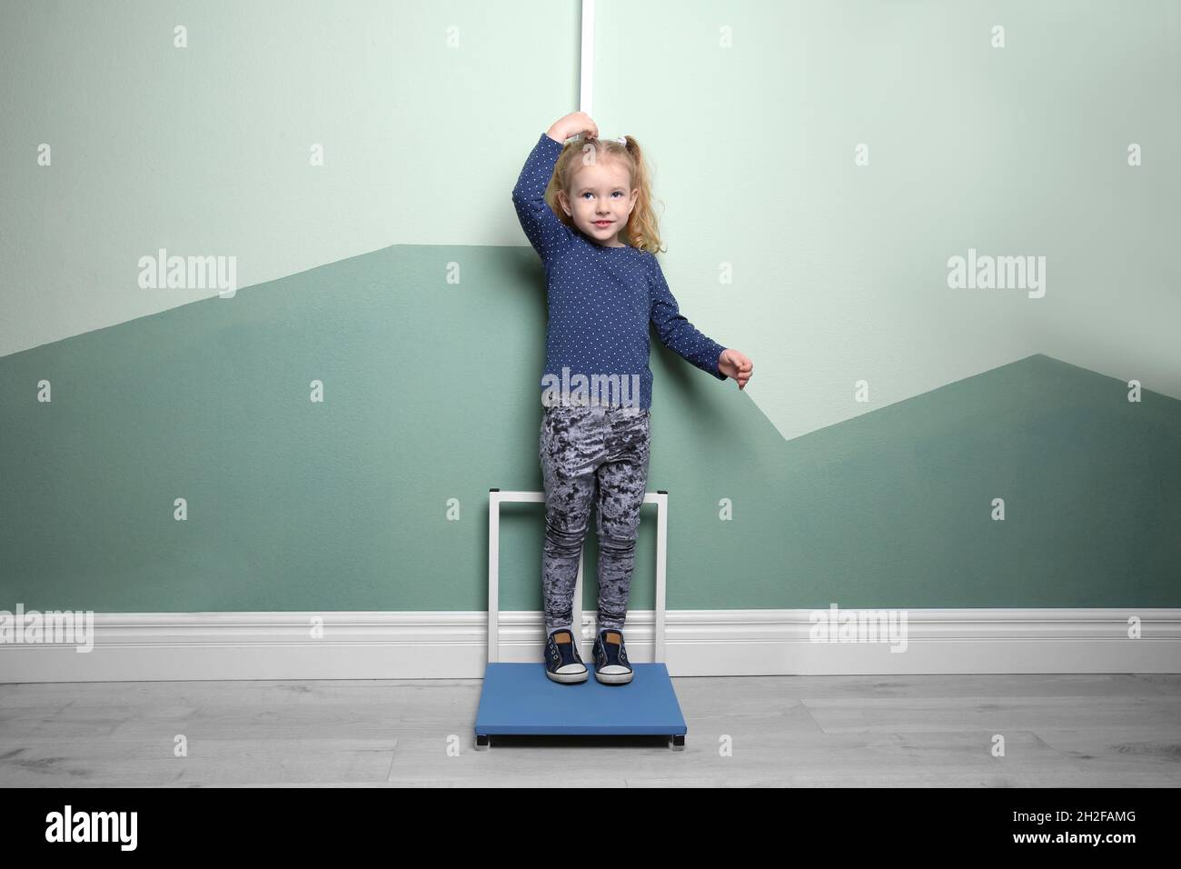 Little girl measuring her height near color wall Stock Photo - Alamy