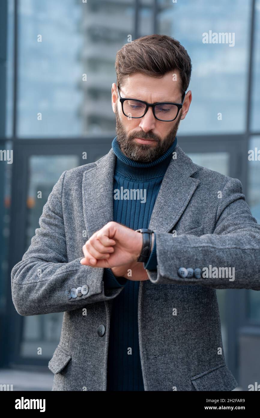 Busy businessman looking at wristwatch while hurrying on meeting stand ...