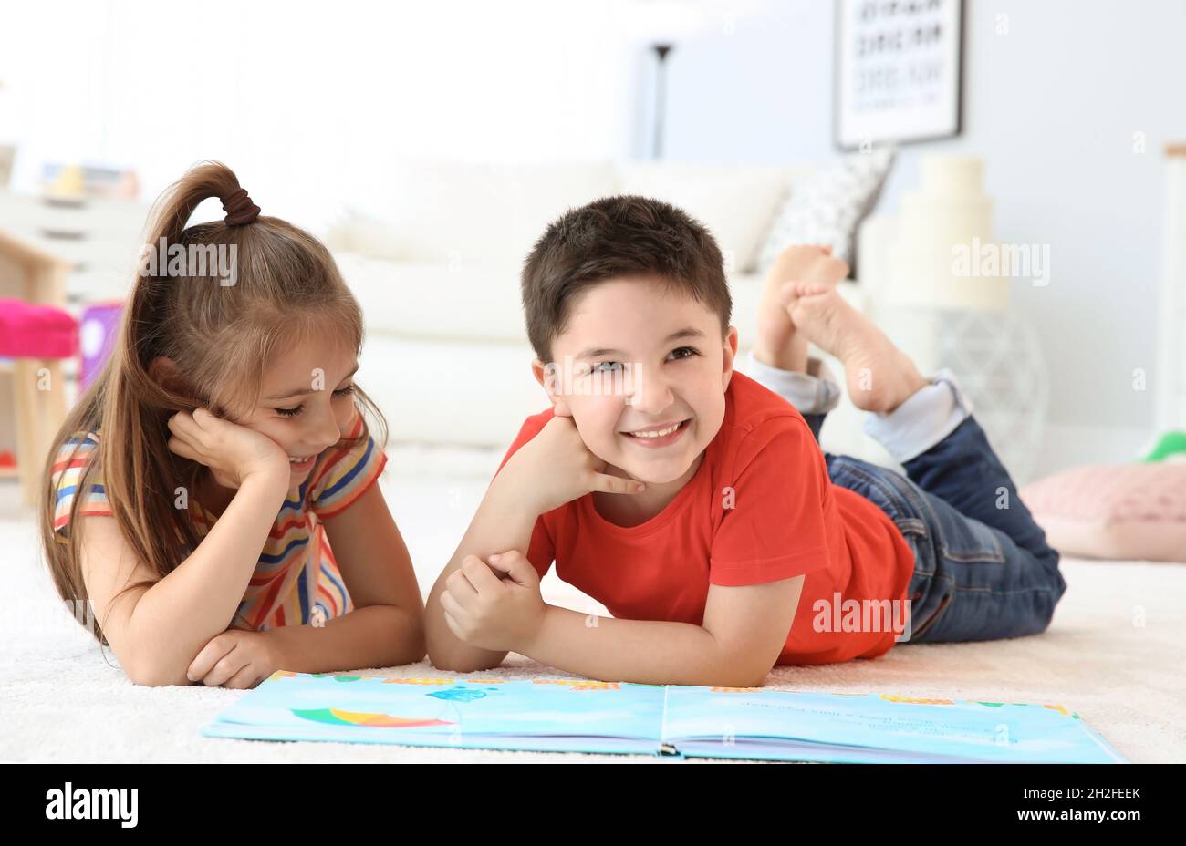 Cute little children reading book on floor in playing room Stock Photo ...