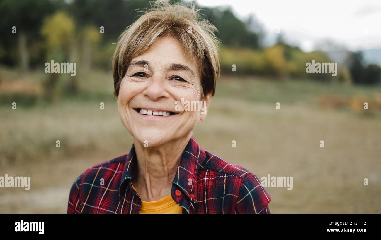 Happy senior woman smiling on camera outdoor in the woods - Focus on ...