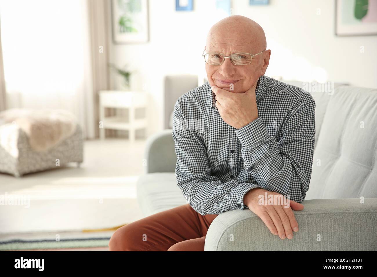 Elderly man sitting on couch in living room Stock Photo - Alamy