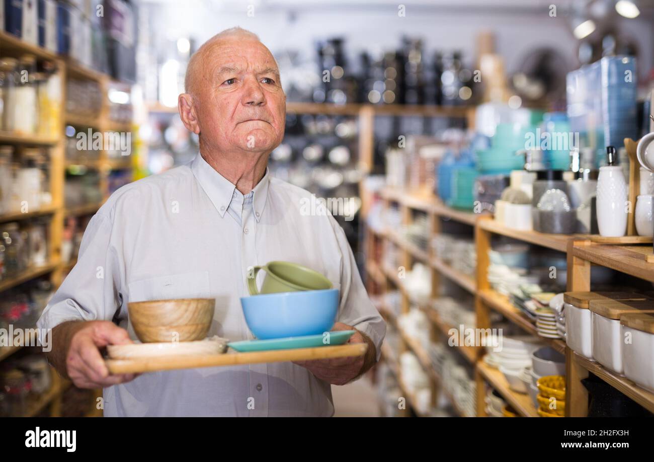 Senior man customer holding purchases and walking in household goods ...