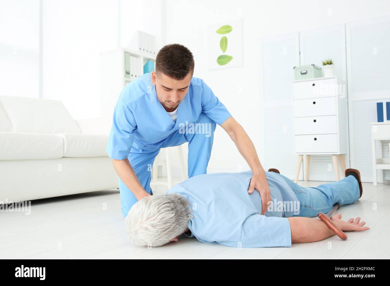 Young doctor giving first aid to senior man with heart attack in clinic ...