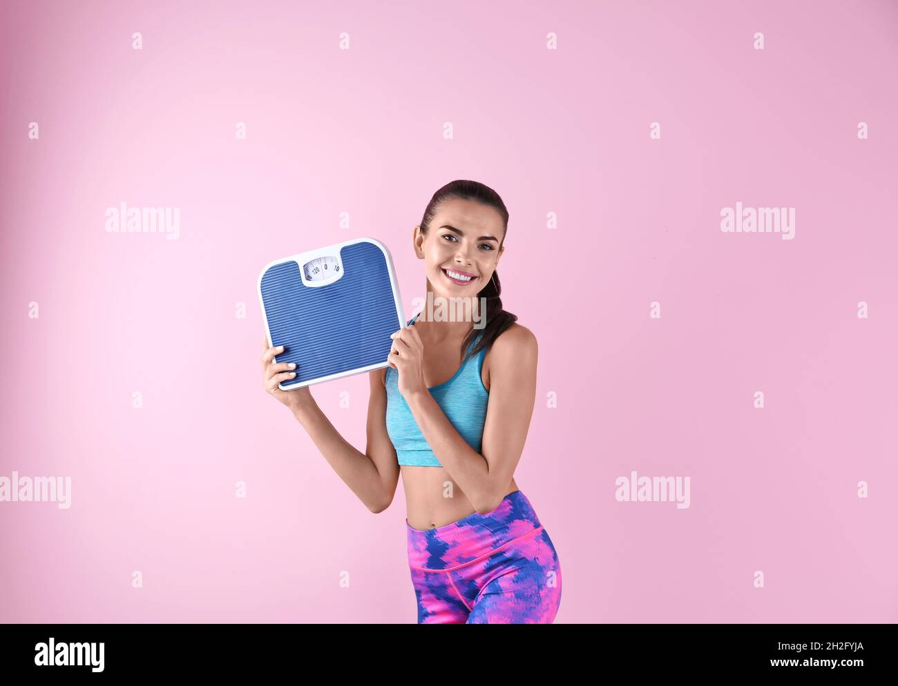 Happy young woman with scales on color background. Weight loss ...