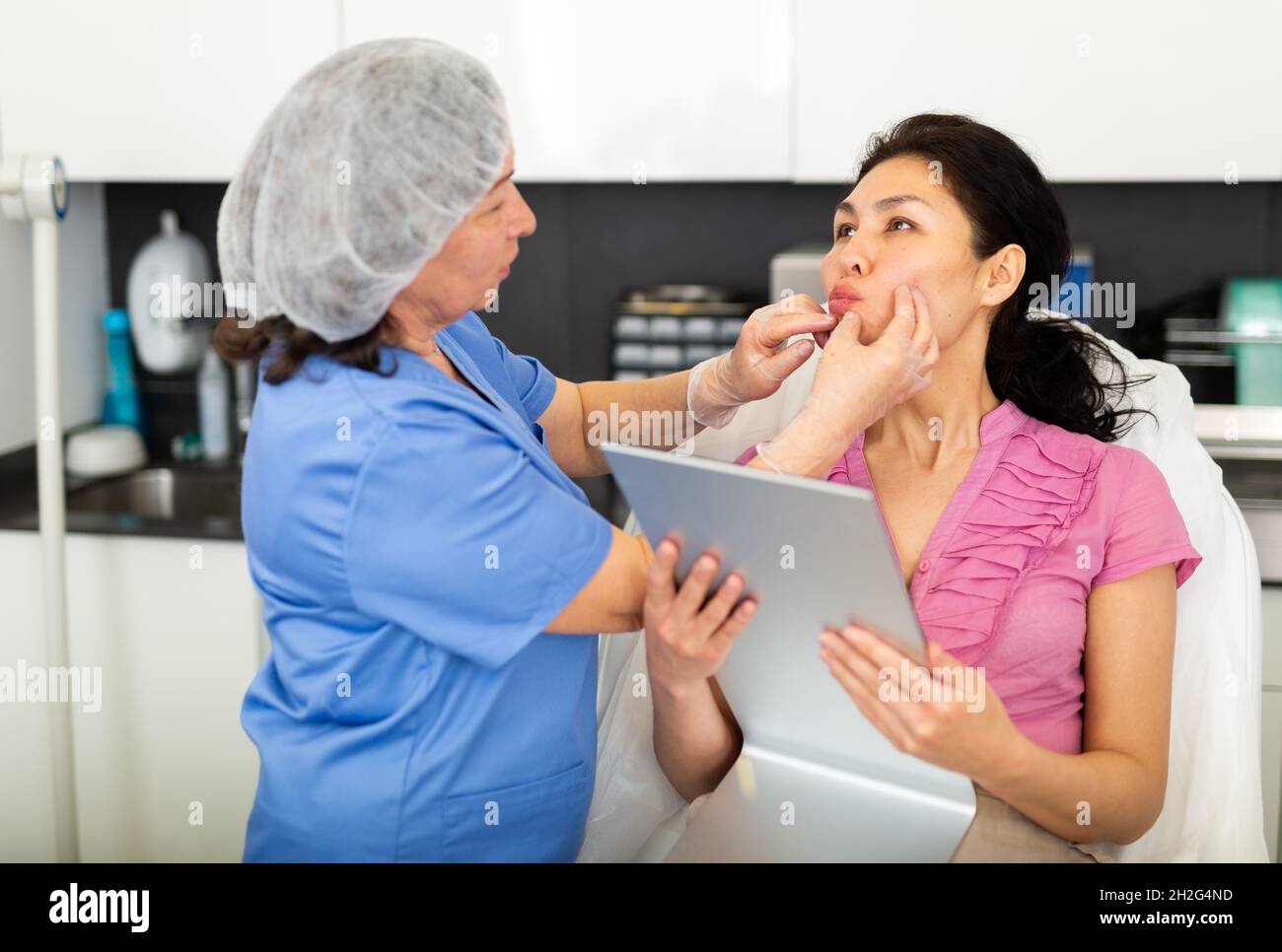 Cosmetologist examining lips of female client before procedure Stock ...