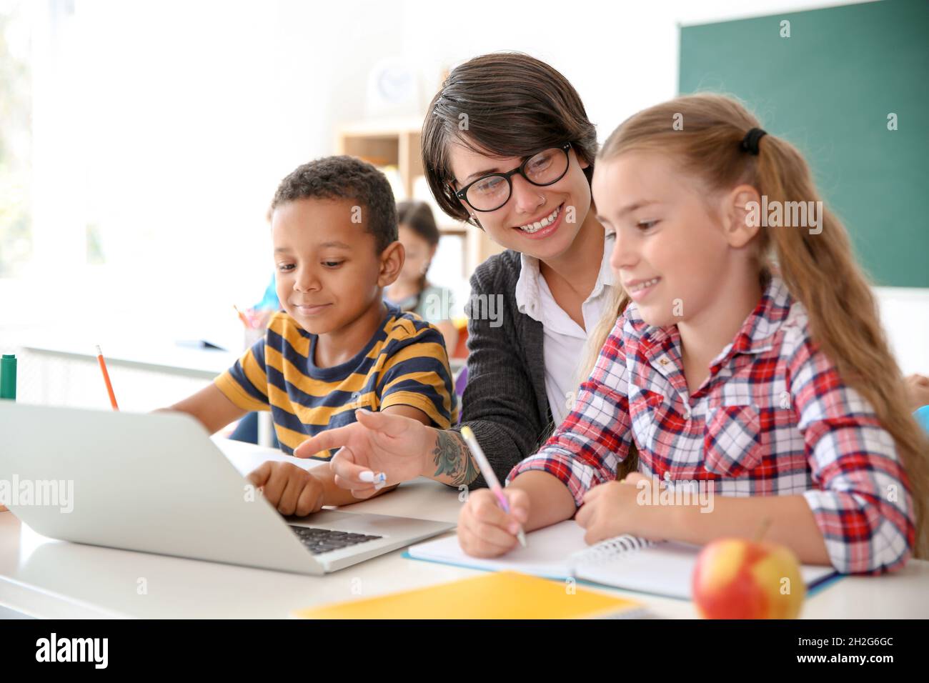 Female teacher helping children with assignment at school Stock Photo ...