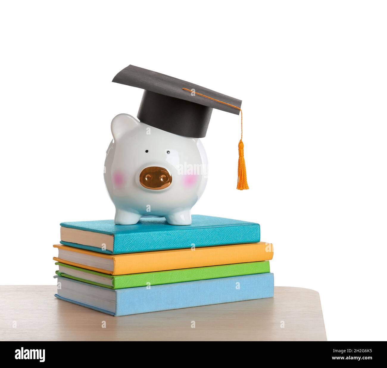 Piggy bank with graduation hat and books on table against white ...