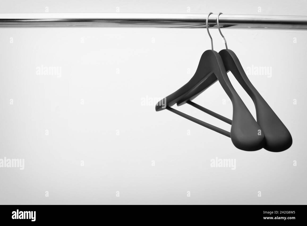 Clothes hangers on metal rail against light background Stock Photo - Alamy