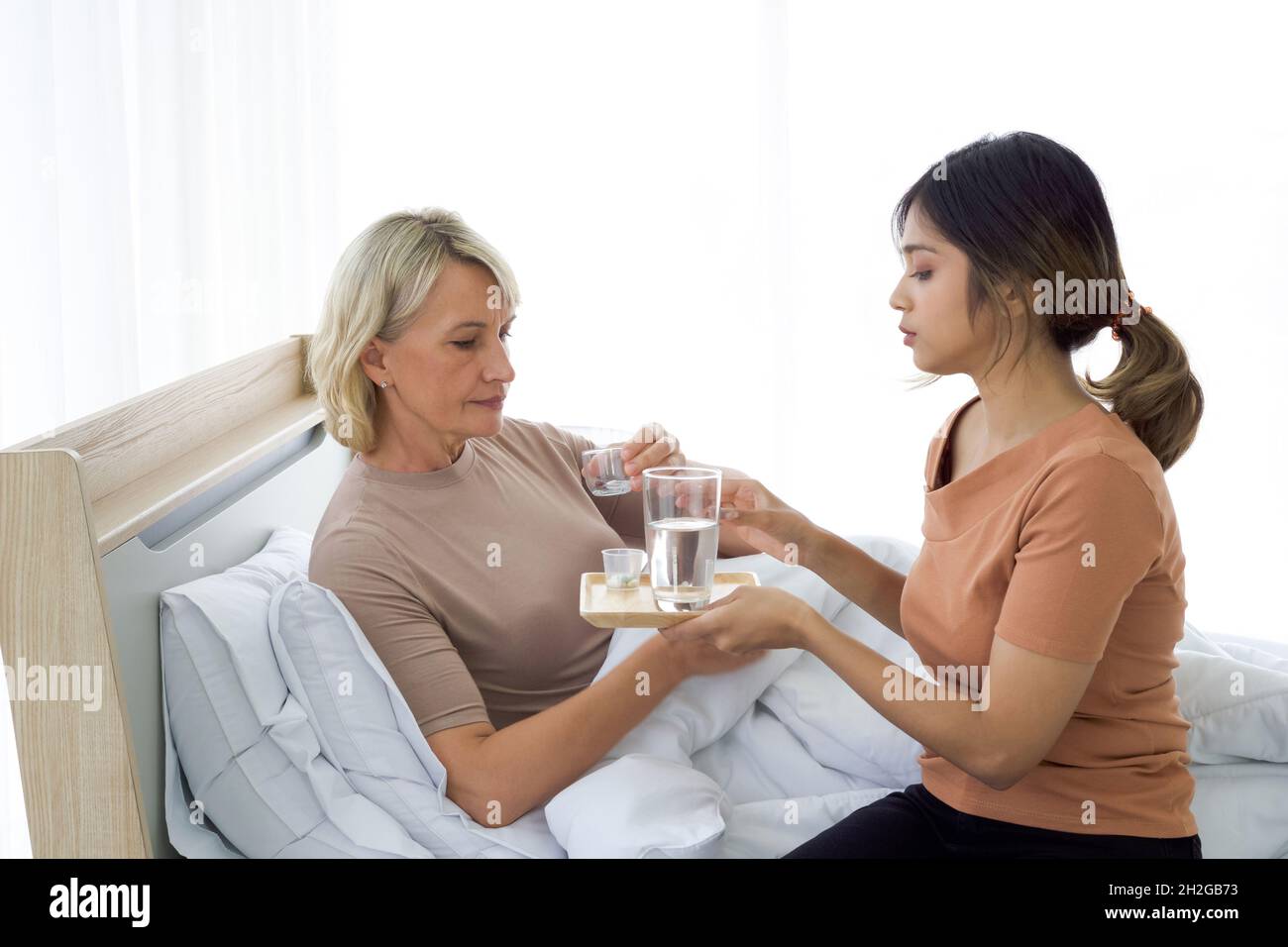 Asian daughter taking care of her sick mother in bed. Senior woman take ...