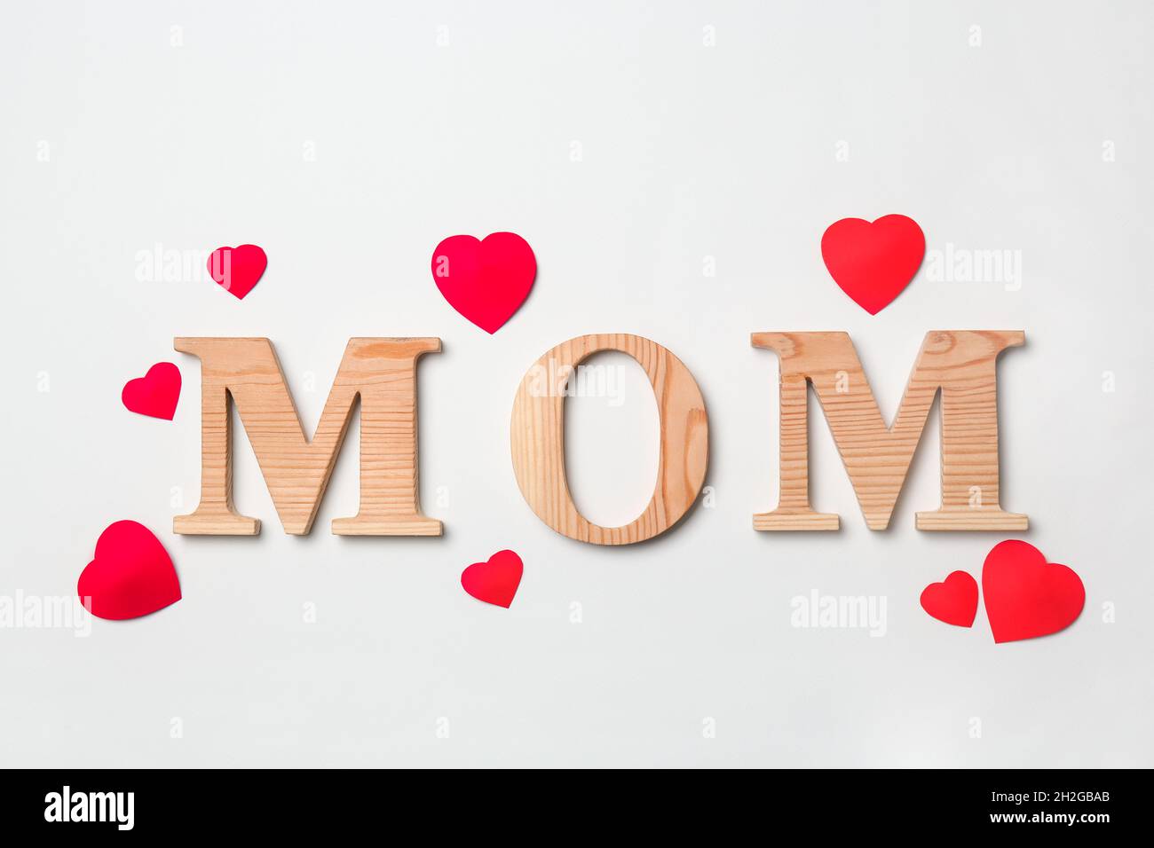 Word "MOM" made of wooden letters and paper hearts on white background ...