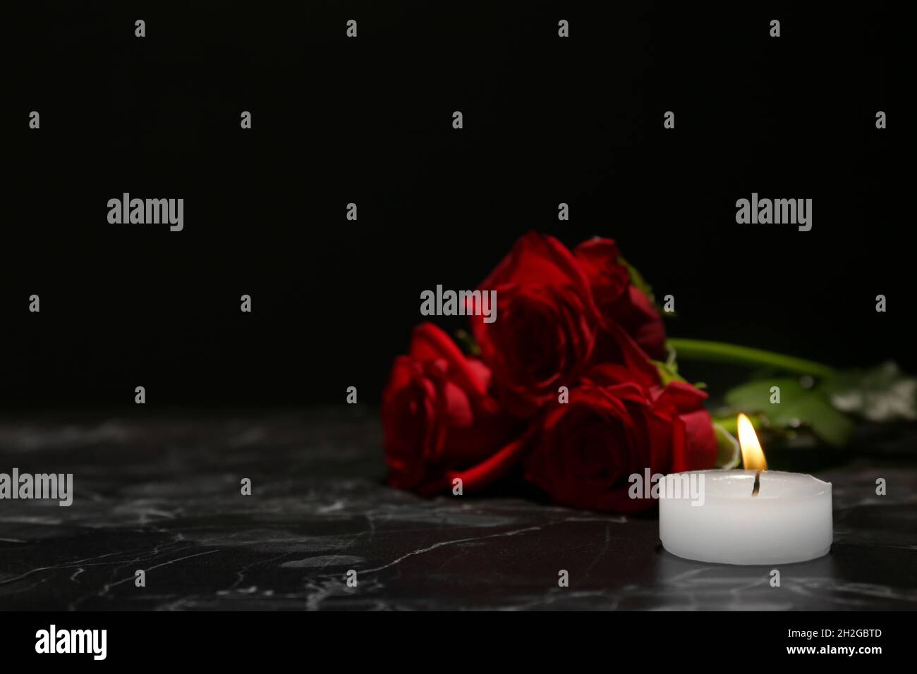 Beautiful red roses and candle on table against black background ...