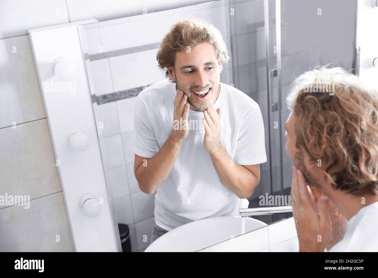 Young man washing face with soap near mirror in bathroom Stock Photo ...