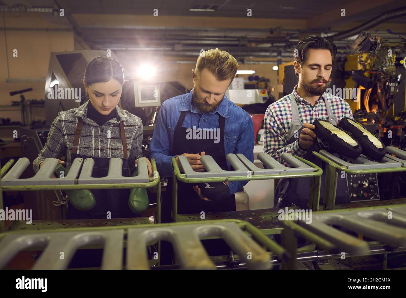 Group of workers making new footwear standing in manufacturing workshop ...