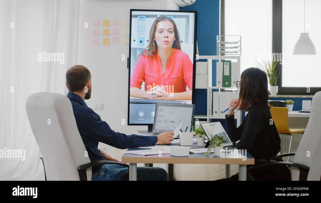 Workmates using video call on television for conversation with woman ...