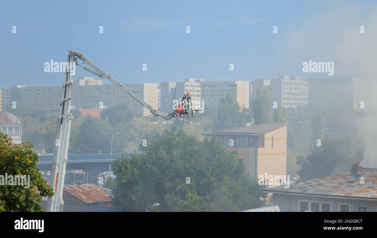Firemen on platform truck going on roof of house on fire. View of ...