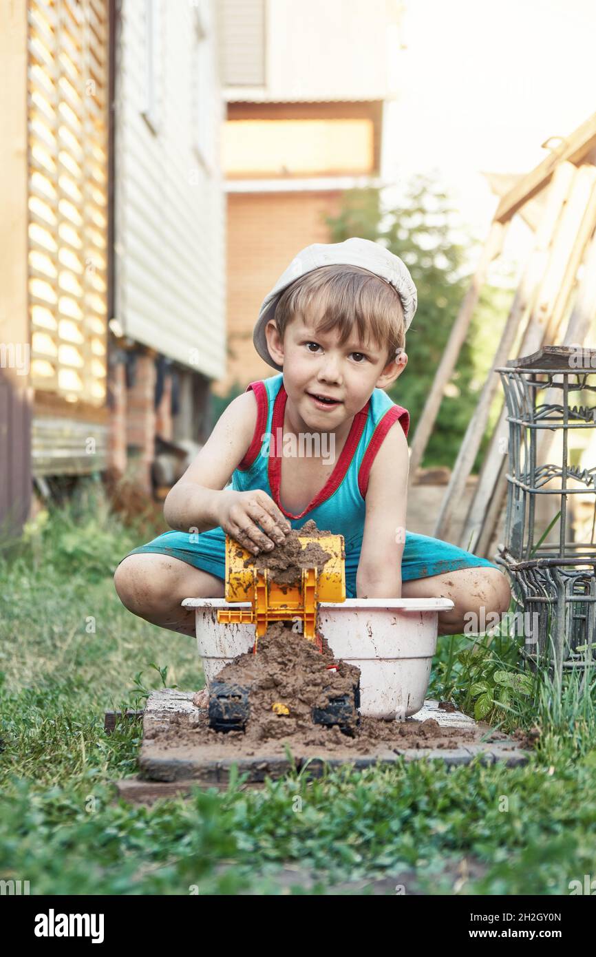 Barefoot little boy puts wet sand into bucket of yellow toy bulldozer ...
