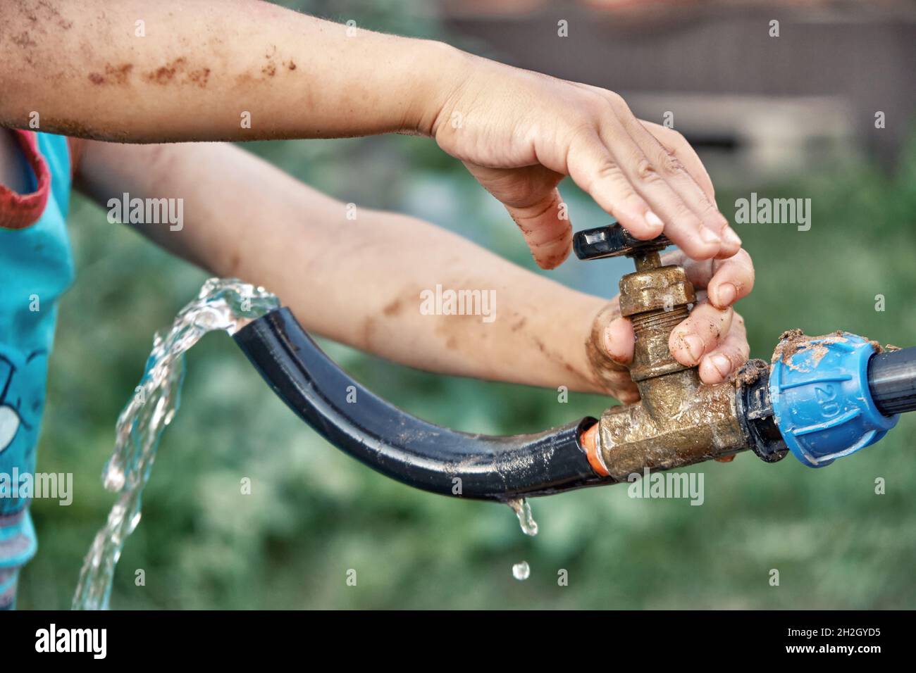 Little kid boy with dirty hands turns lever on tap with hose and ...