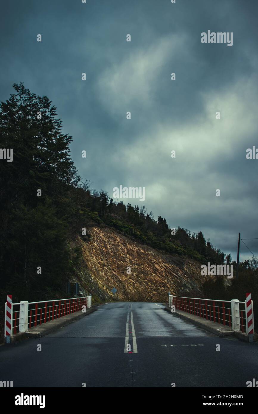 Eerie scenery of an empty road by the cliff under heavy gray clouds ...
