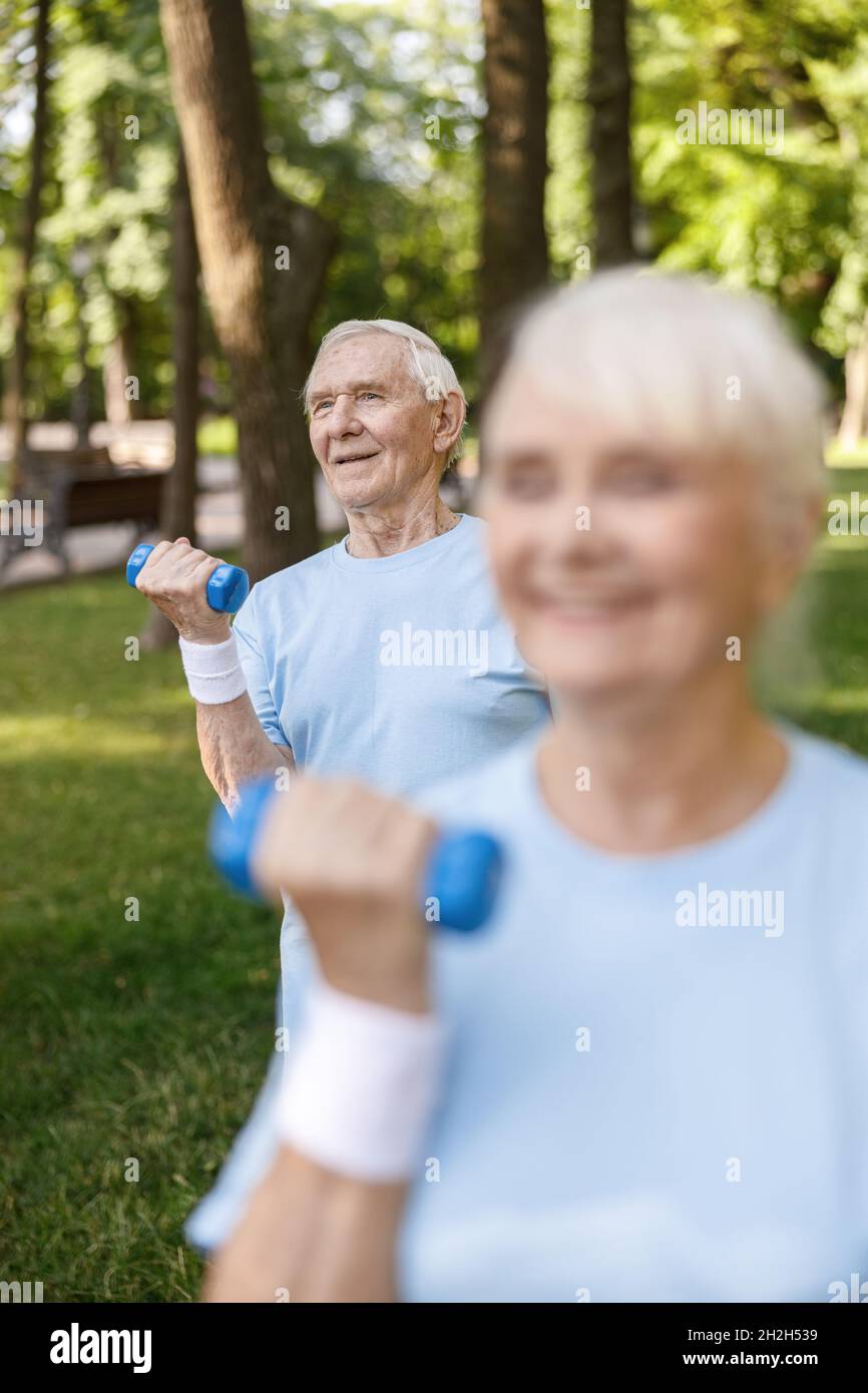 Happy senior gentleman does exercises with dumbbell training with wife ...