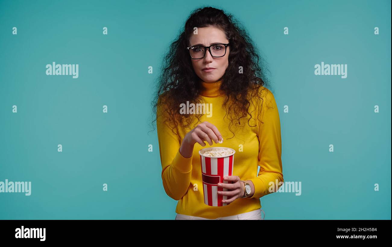curly young woman watching movie and holding popcorn bucket isolated on ...