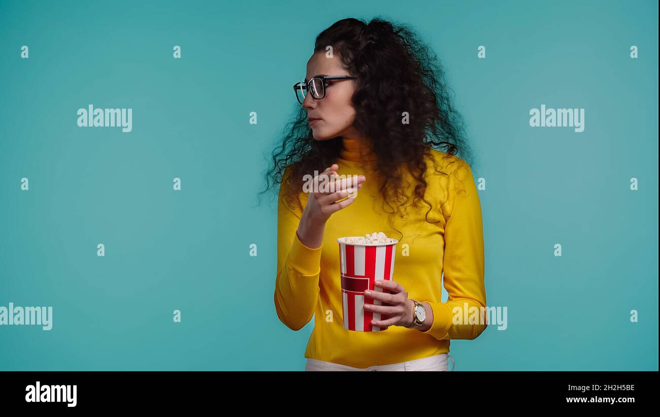 curly young woman holding popcorn bucket isolated on turquoise Stock ...