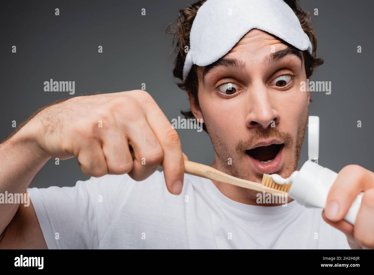 Shocked man in sleep mask pouring toothpaste on toothbrush isolated on ...