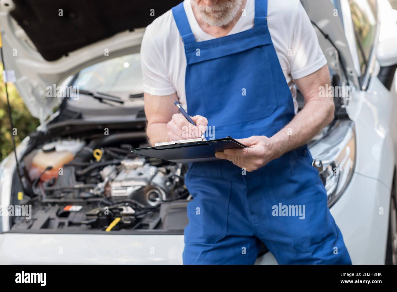Car mechanic checking a car engine and writing on clipboard Stock Photo ...
