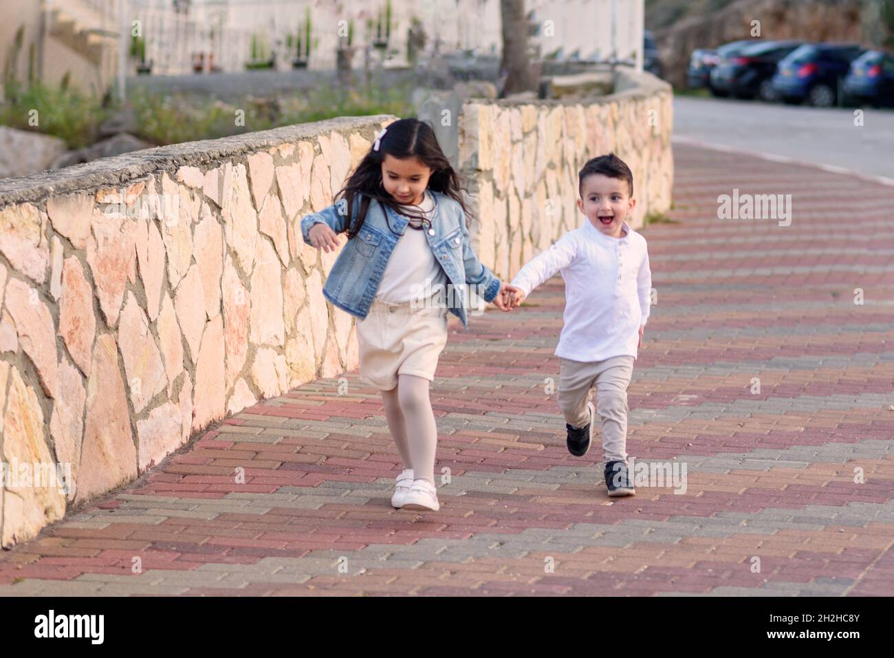 Two cute young preschool children running and playing in a city street ...