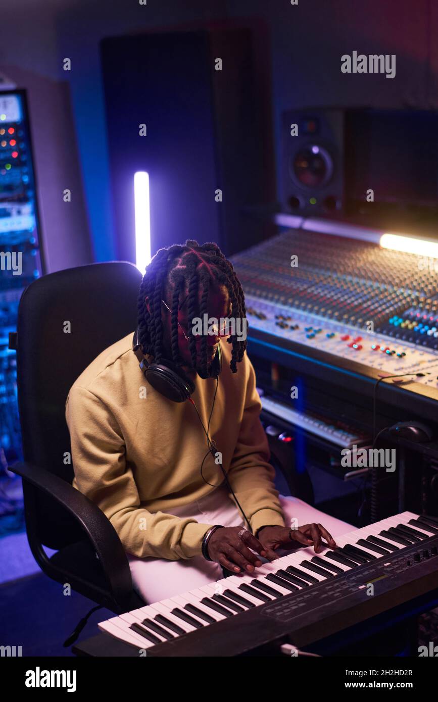 African young composer in headphones playing piano to write music in ...