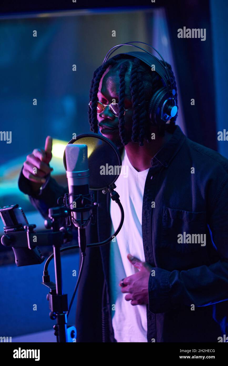 African young singer in headphones singing to microphone, he writing a ...