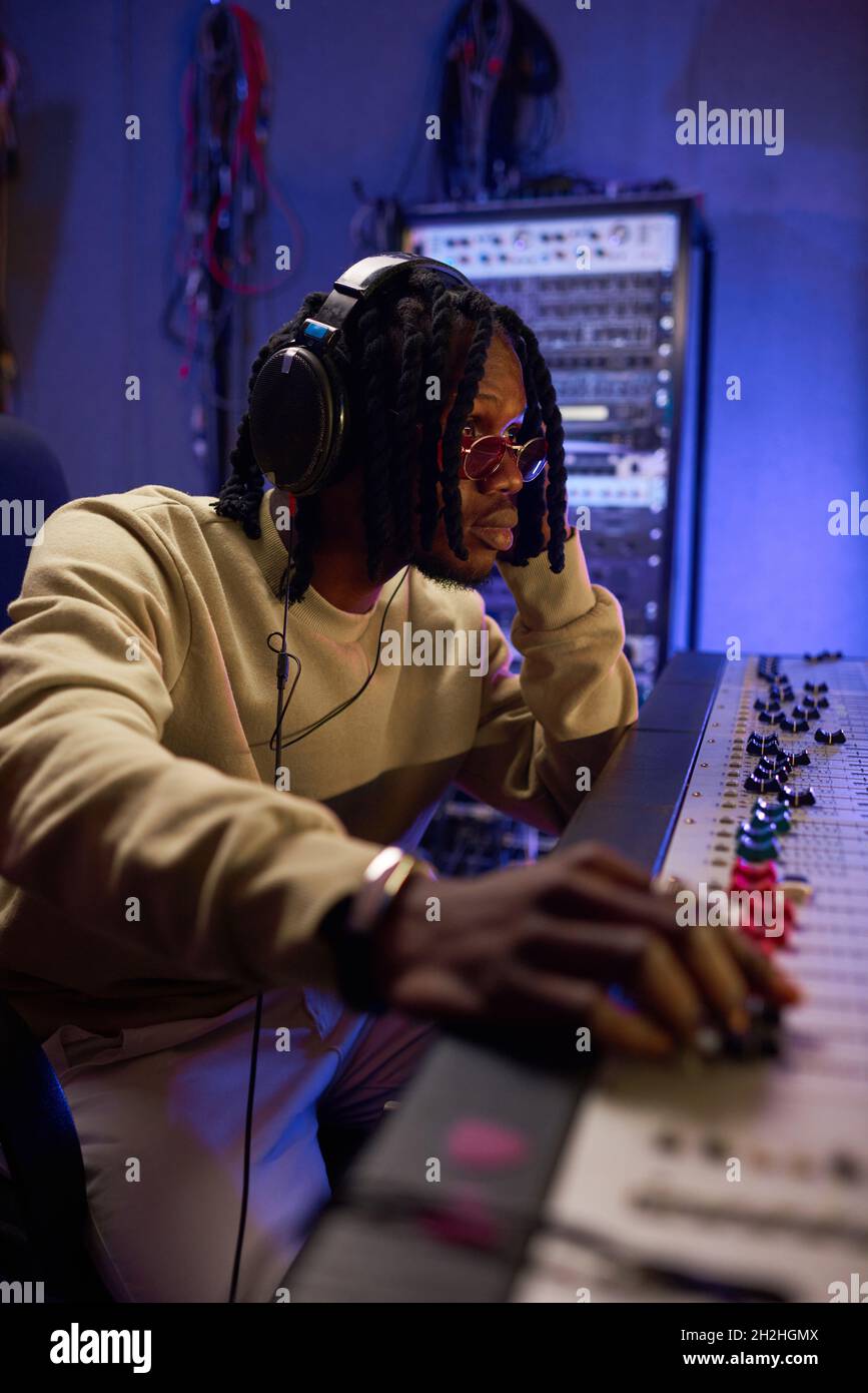 African young musician in headphones using music keyboard to compose ...