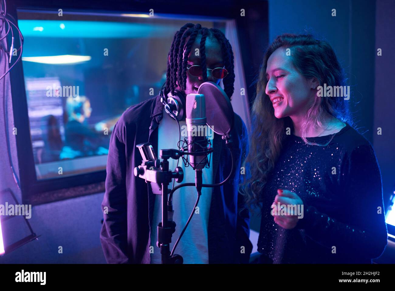 Young multiethnic couple singing to microphone together while recording ...