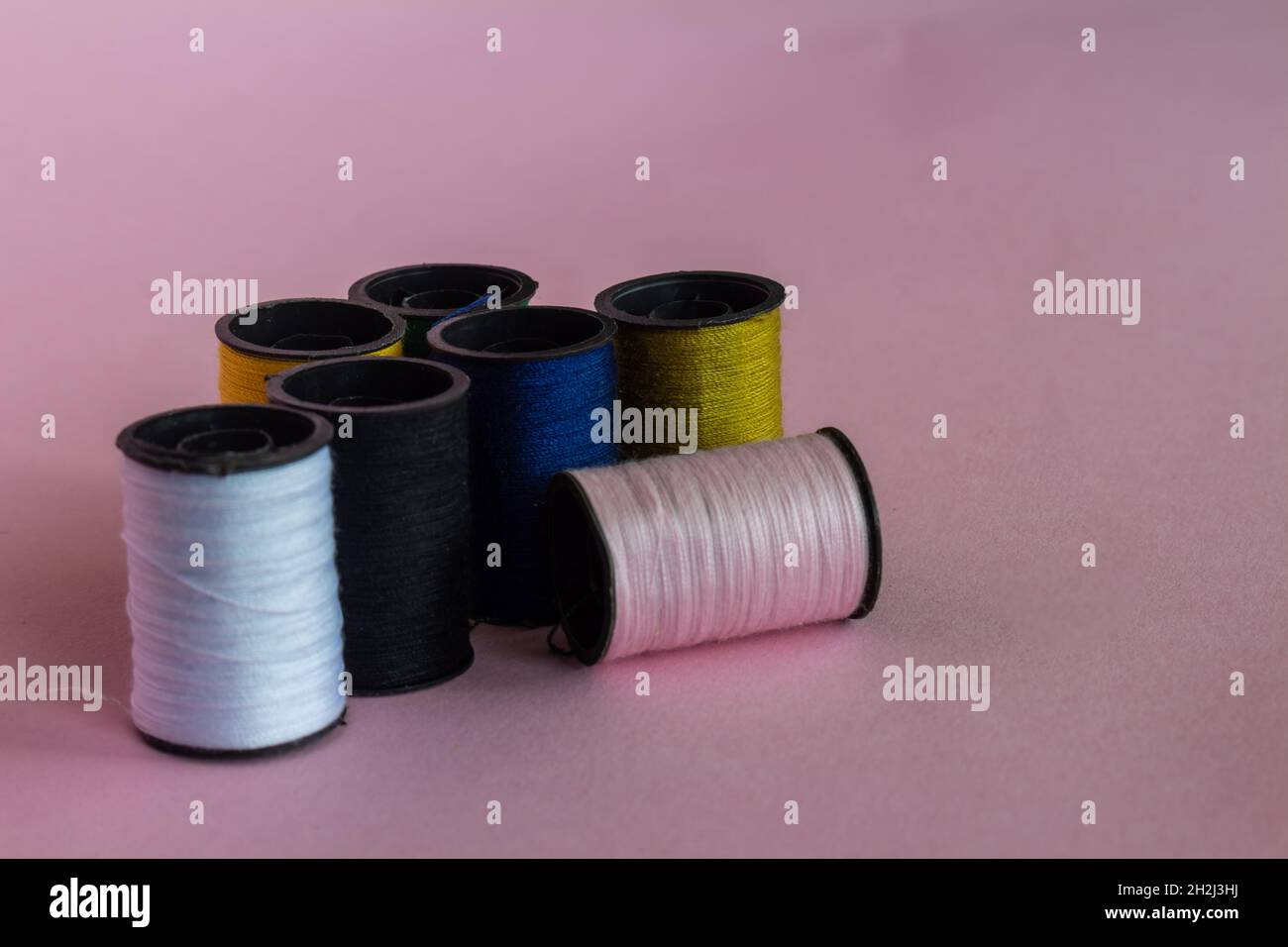 Black plastic spools containing multi-colored thread on a neutral pink ...