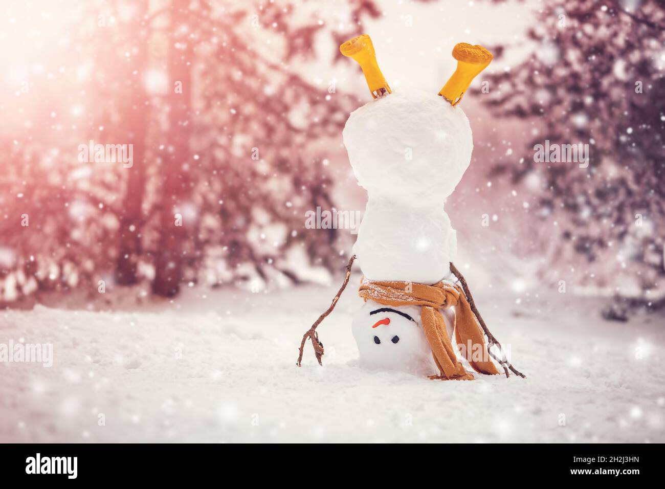 Cheerful snowman with orange scarf and in yellow boots stands upside ...