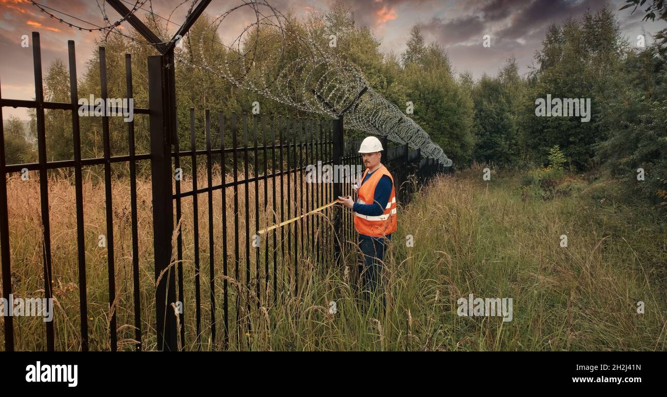 Worker with a measuring tape measure a fence with barbed wire Stock ...