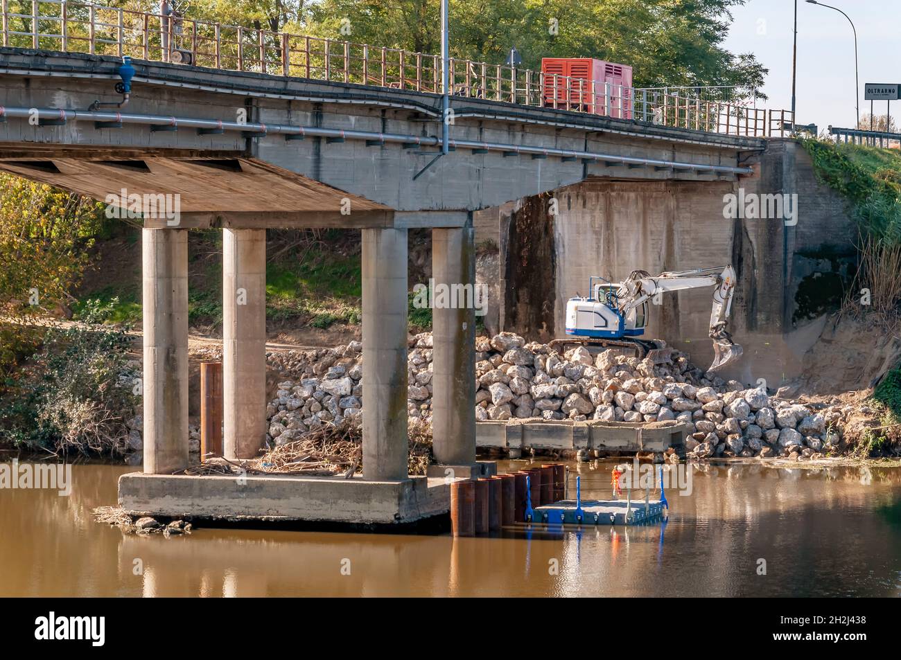 A white excavator works under a bridge over the Arno river to reinforce ...