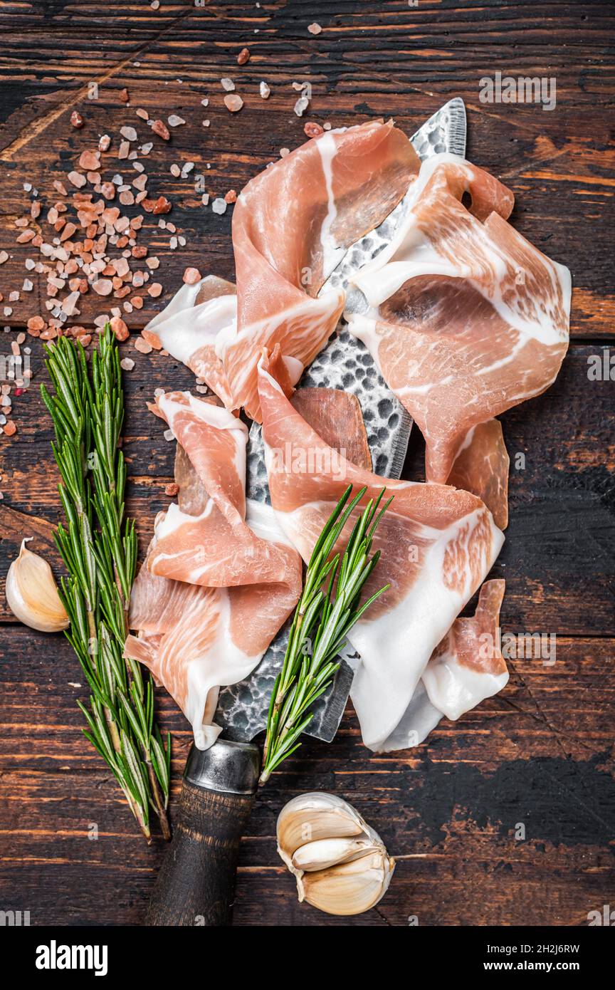 Dry cured Prosciutto crudo parma ham on a butcher knife. Dark wooden ...