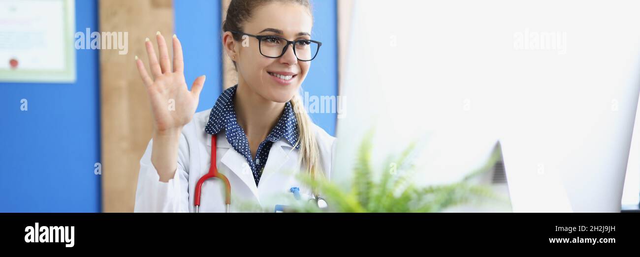 Woman doctor in glasses waving hand at laptop screen in clinic Stock ...