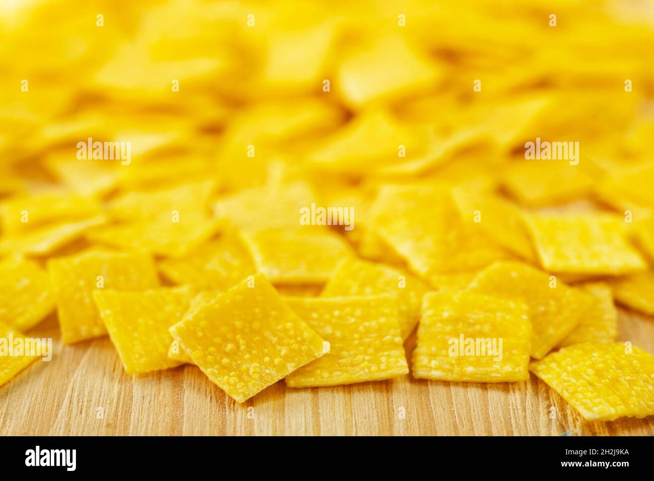 Pile of small flat squares of egg pasta called quadrucci on wooden ...