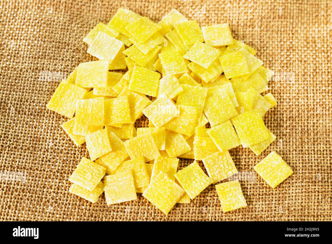 Pile of small flat squares of egg pasta called quadrucci on sackcloth ...