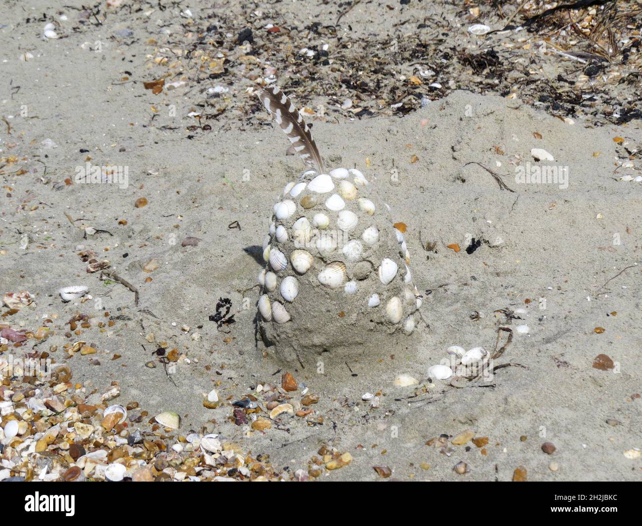 a sandcastle on the beach decorated with sea shells and a feather Stock ...