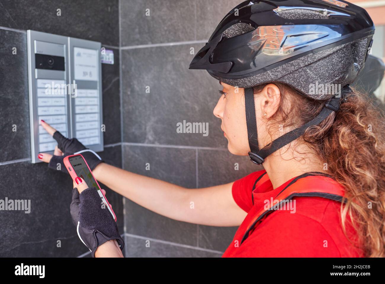 A cyclist delivery girl ringing the intercom bell Stock Photo - Alamy