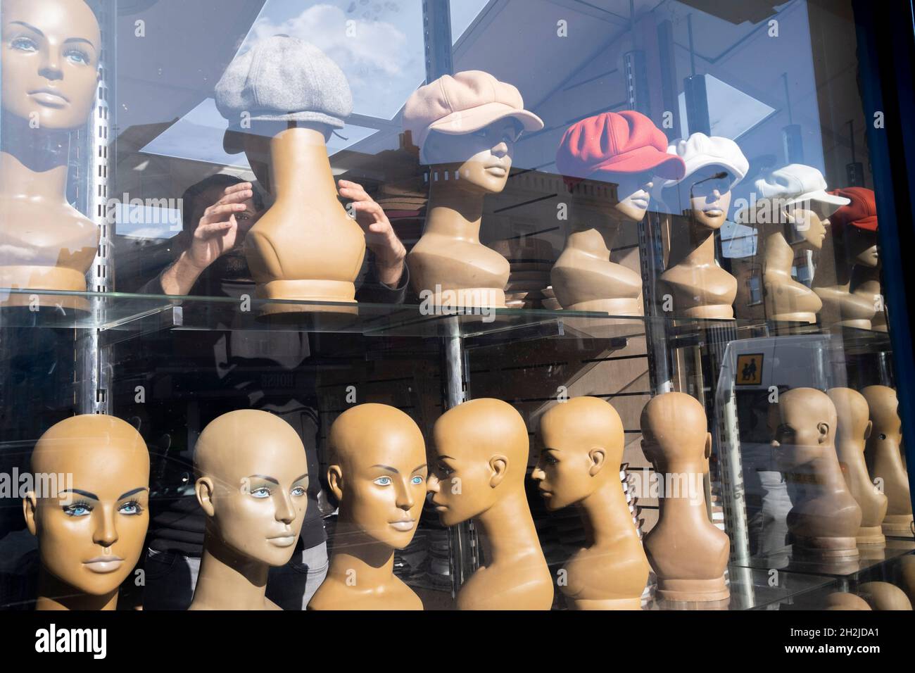 A shopkeeper fits and adjusts the hats on female mannequin heads in the ...