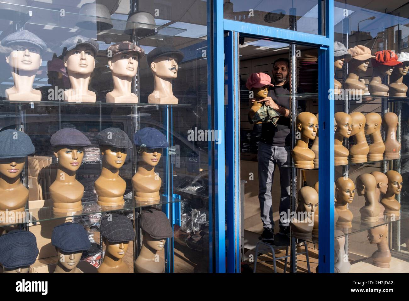 A shopkeeper fits and adjusts the hats on female mannequin heads in the ...